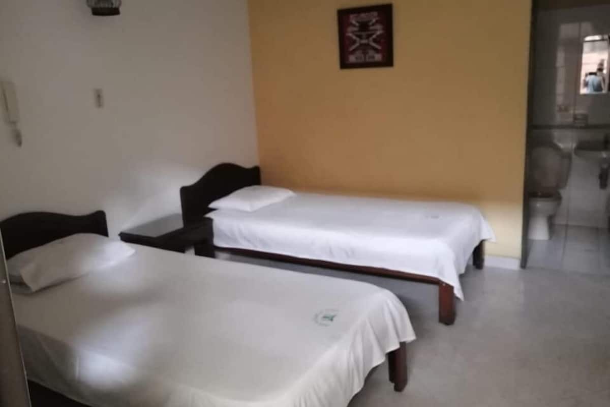 Quarto com duas camas de solteiro, uma mesinha, telefone fixado na parede e um quadro emoldurado.
