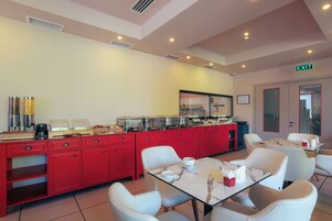 Espaço de café da manhã com buffet, assentos e sinalização de saída.