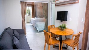 Quarto de hotel moderno com sofá, mesa de jantar com cadeiras, televisão e varanda com cama.