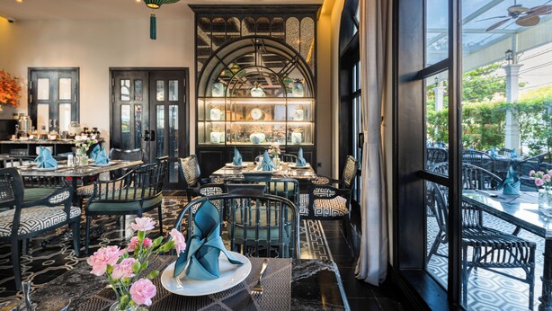 Um restaurante com decoração moderna, destacando um chão em padrão preto e branco, mesas e cadeiras organizadas e vista para o exterior através de grandes janelas.