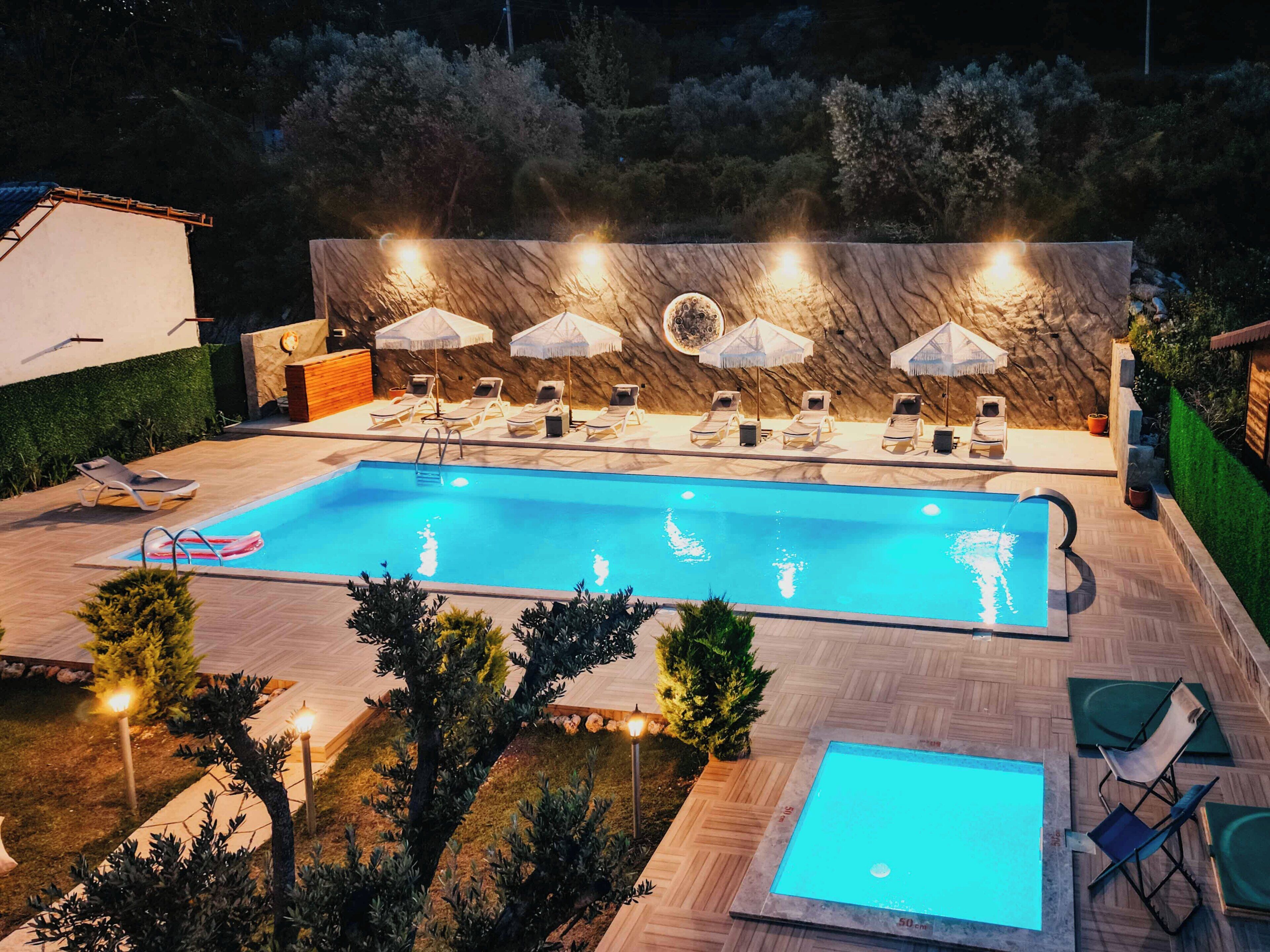 Piscina retangular com espreguiçadeiras e guarda-sóis, cercada por um deck de madeira e vegetação.