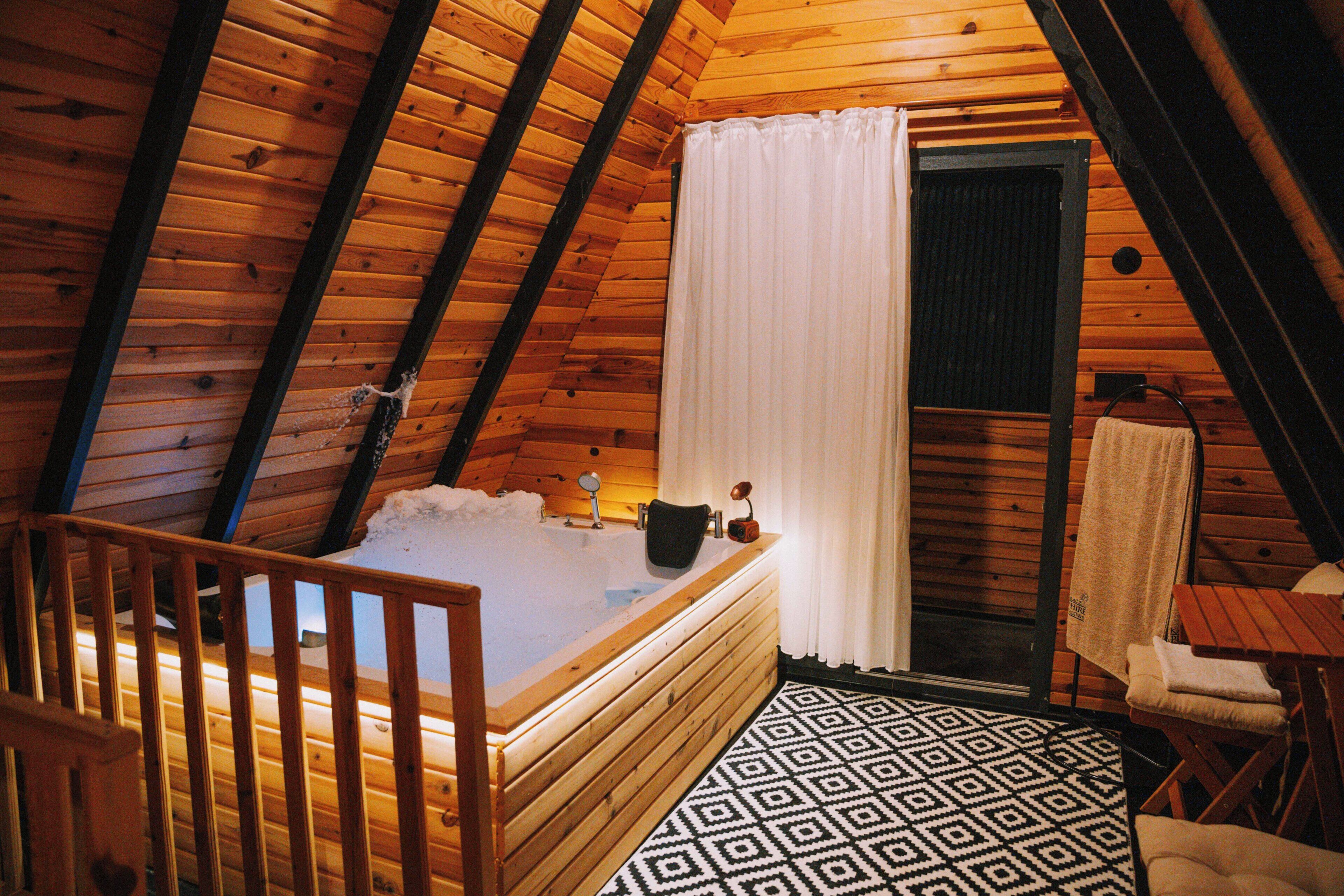 Uma cabana de madeira com uma banheira de madeira, um chão estampado e uma pequena mesa com uma toalha.