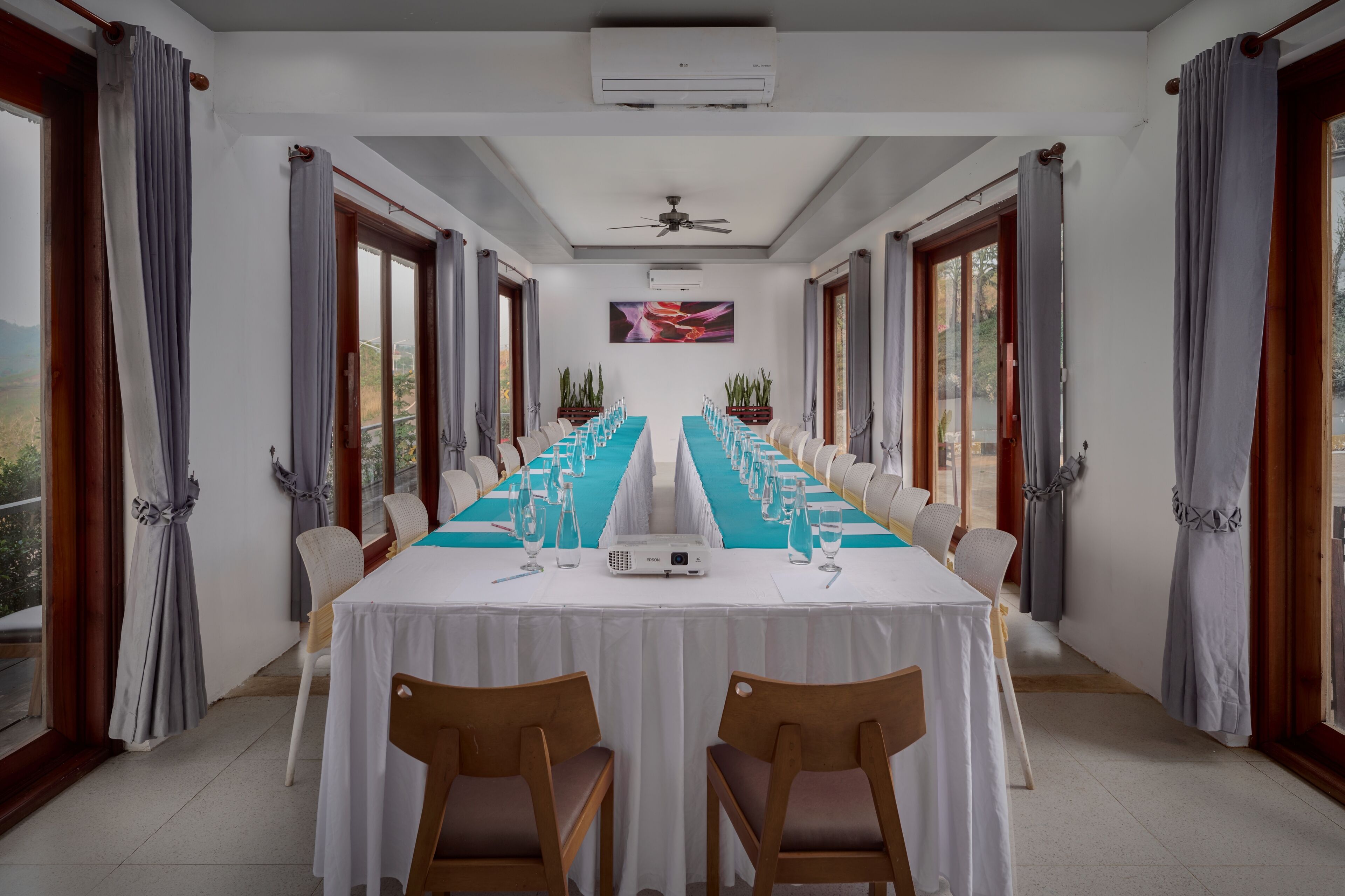 Uma sala de conferências com uma mesa comprida, cadeiras, um projetor e cortinas.