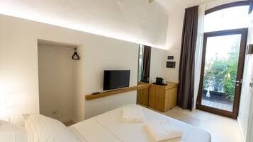 Quarto de hotel com cama, televisão, secretária com computador e porta de vidro deslizante para uma varanda.