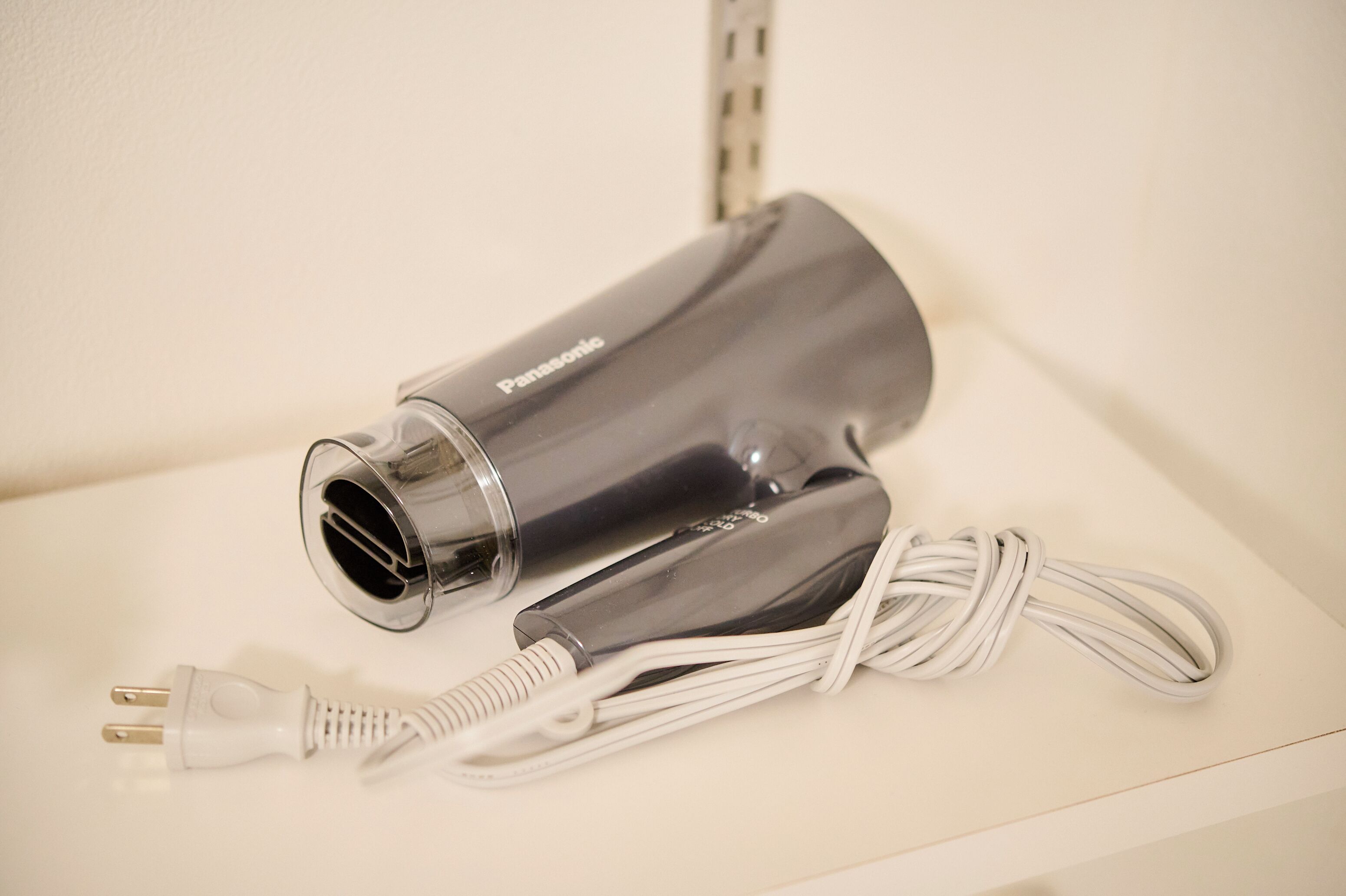 Um secador de cabelo Panasonic com um fio de energia branco sobre uma superfície branca.