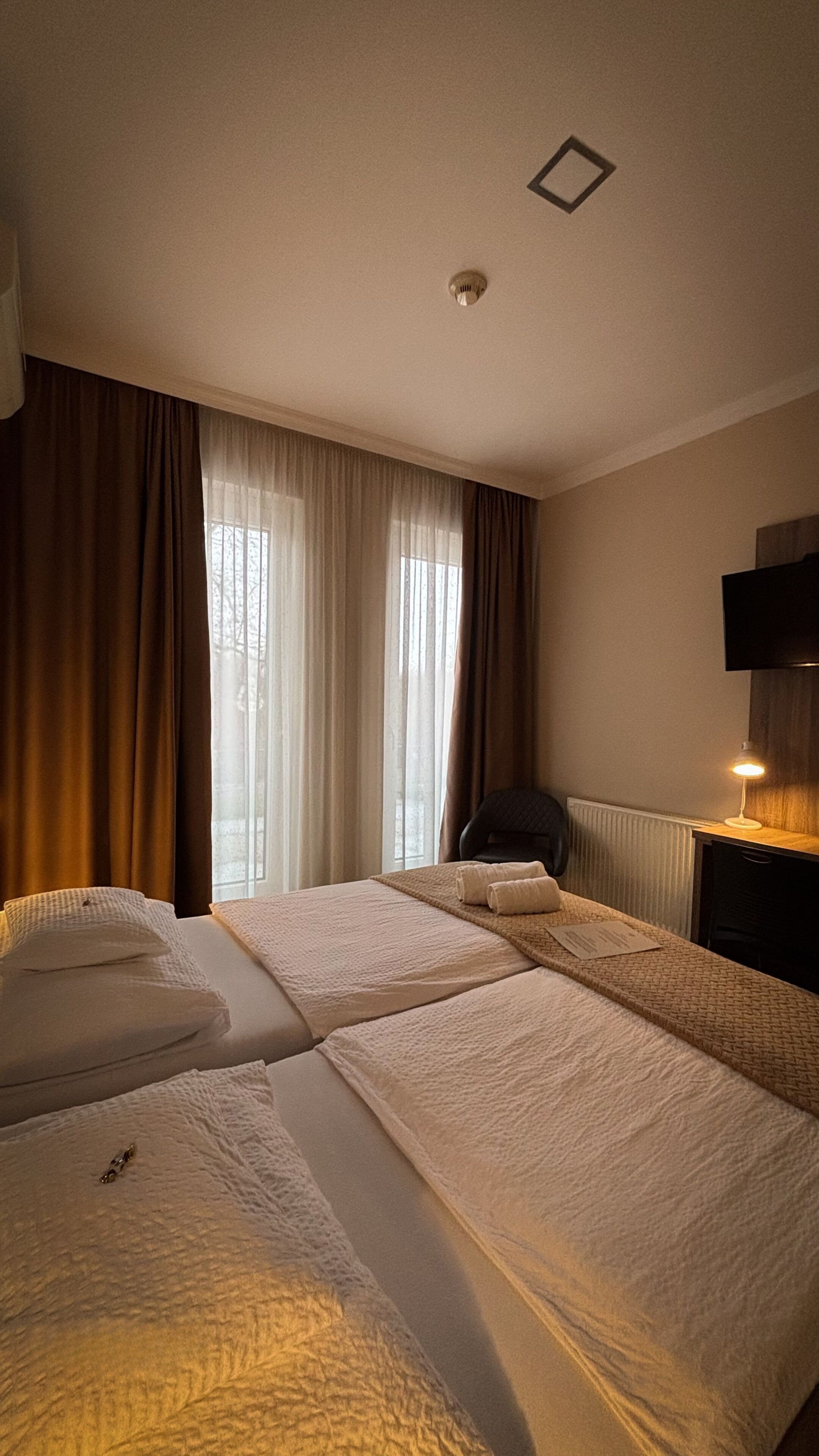 Quarto de hotel com duas camas, uma cadeira, escrivaninha com luminária e televisão na parede.