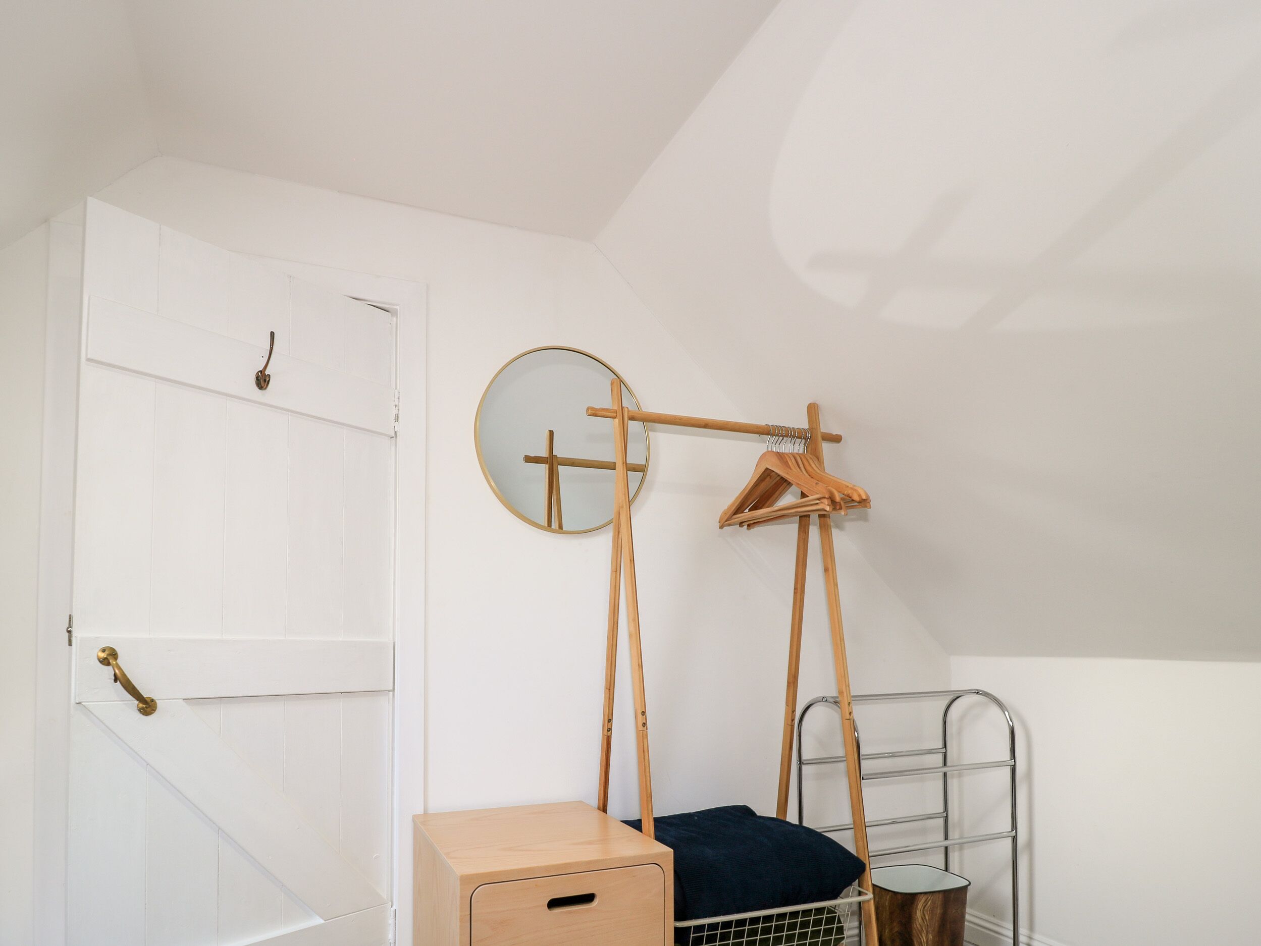 Um quarto com porta branca, cômoda de madeira, suporte de metal e espelho na parede.