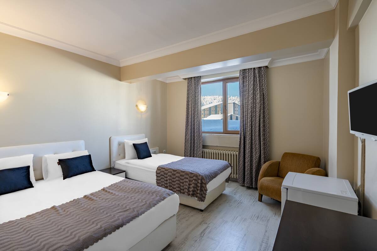 Quarto de hotel com duas camas, um sofá, uma televisão e uma janela com cortinas.