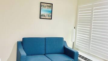 Sala de estar com sofá azul, mesa de centro de madeira, quadro pendurado na parede e janela com persianas.