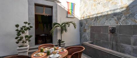 Uma área de refeições ao ar livre com um muro de pedra, uma bandeira e a entrada de um restaurante.