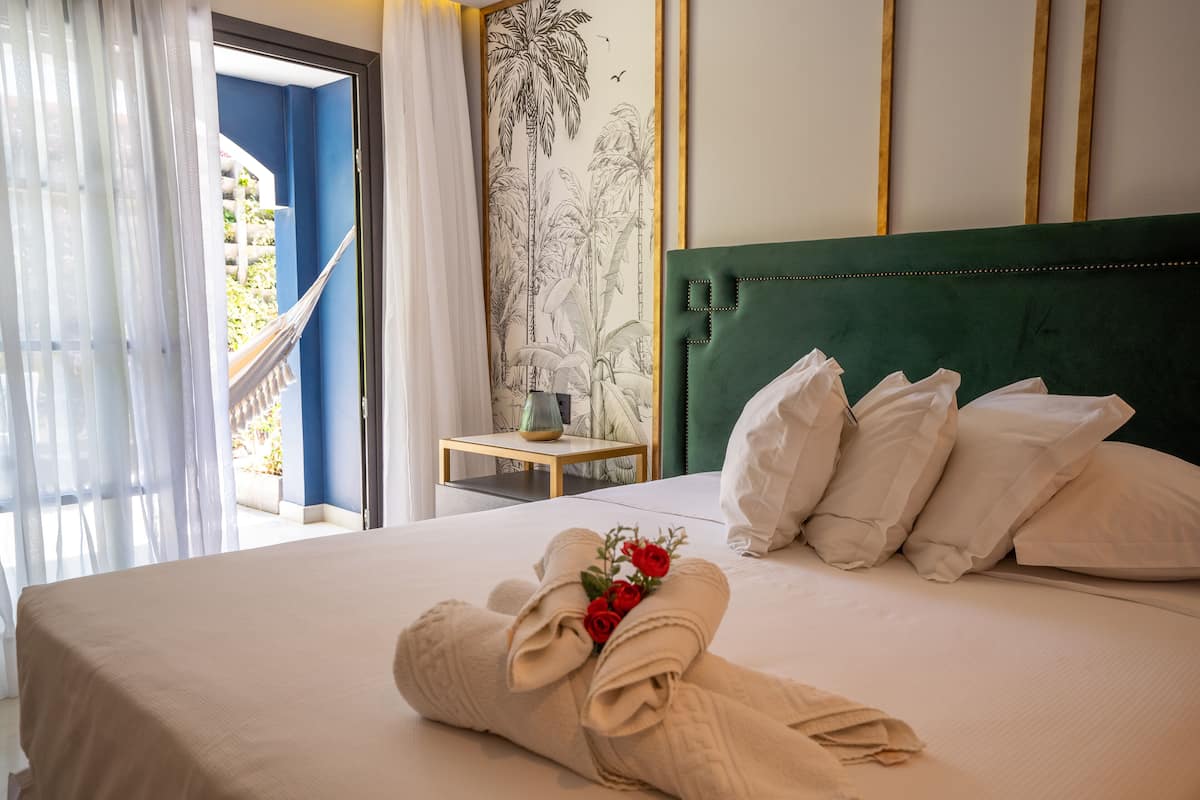 Cama bem arrumada com cabeceira verde, almofadas brancas e toalha com rosas vermelhas.