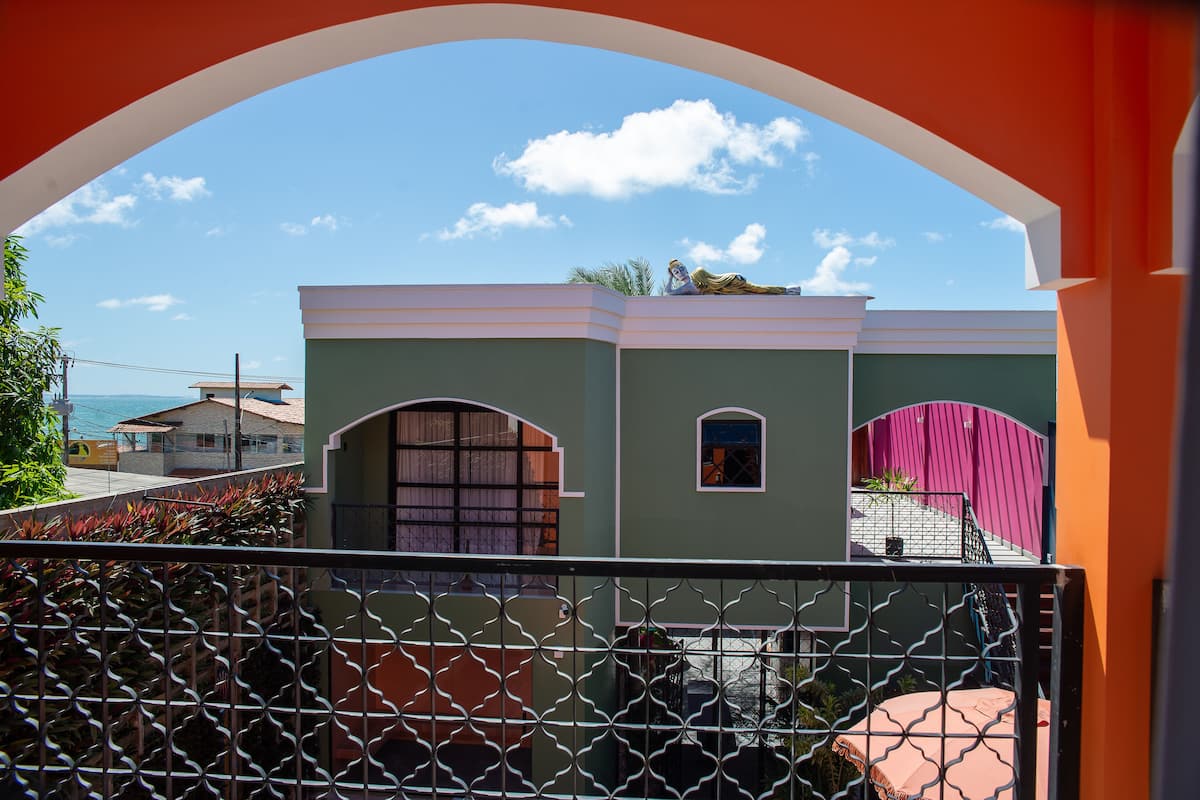 Visão através de um portão de metal de um edifício com fachada verde, toldo rosa e uma pequena janela.