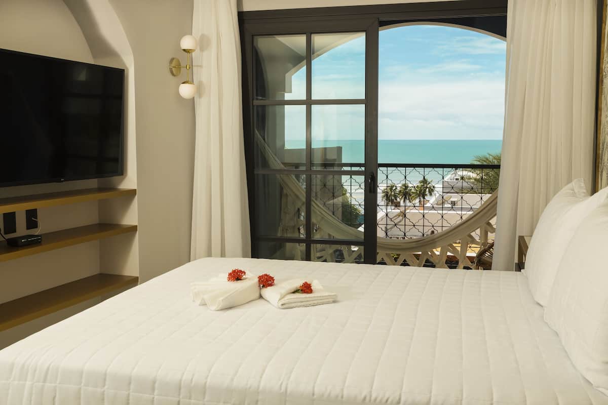 Quarto de hotel com cama, televisão e varanda com vista para o mar.