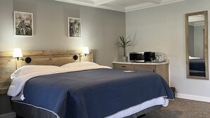 Quarto bem arrumado com cama, abajures, televisão e espelho.