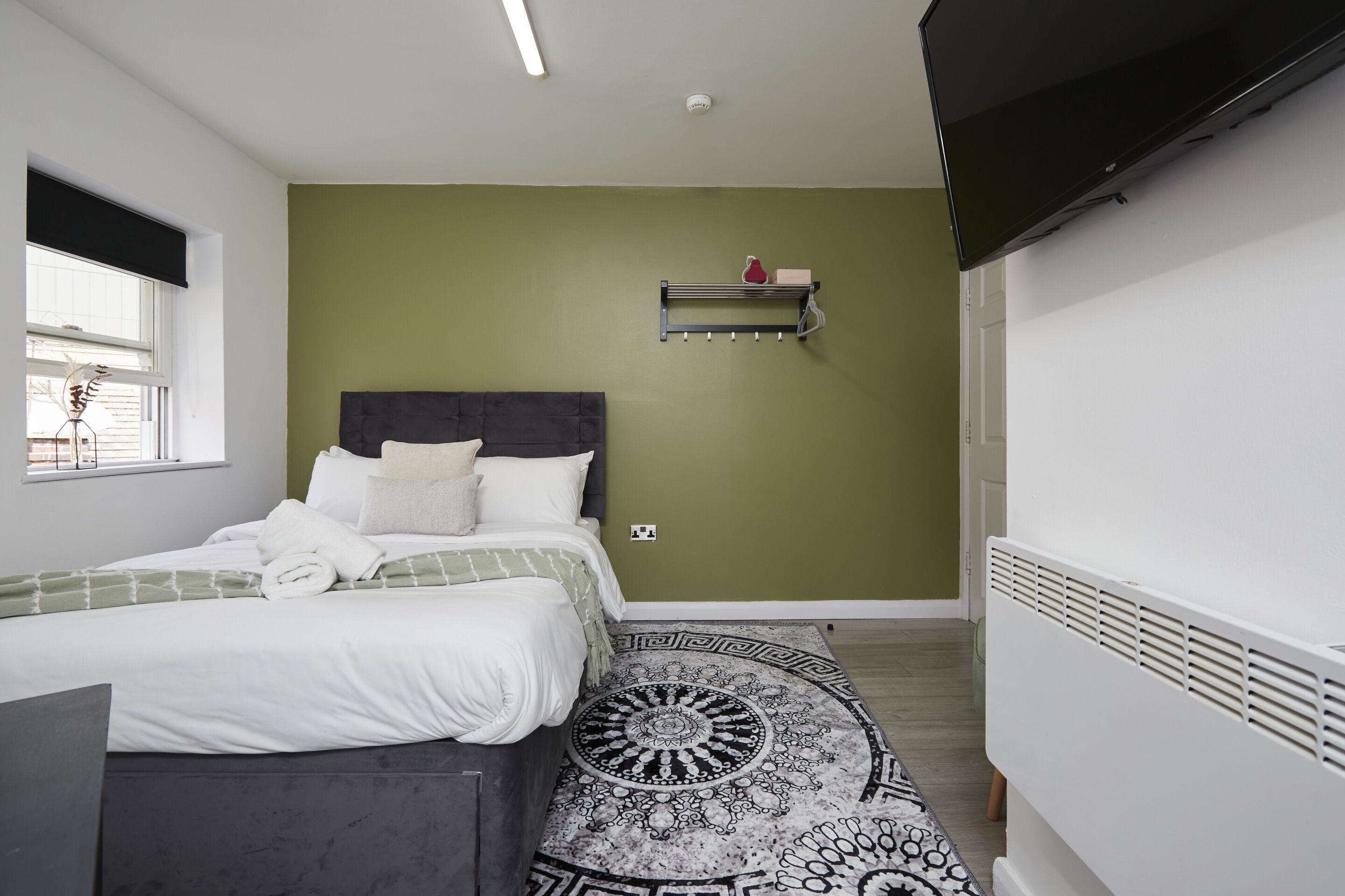 Quarto moderno com cama, prateleira na parede e televisão.