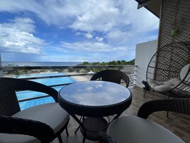Varanda com mesa redonda e cadeiras, vista para uma piscina e o mar.