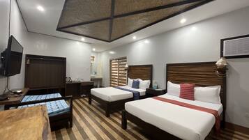 Quarto de hotel com duas camas, uma escrivaninha, uma televisão e um ventilador de teto.