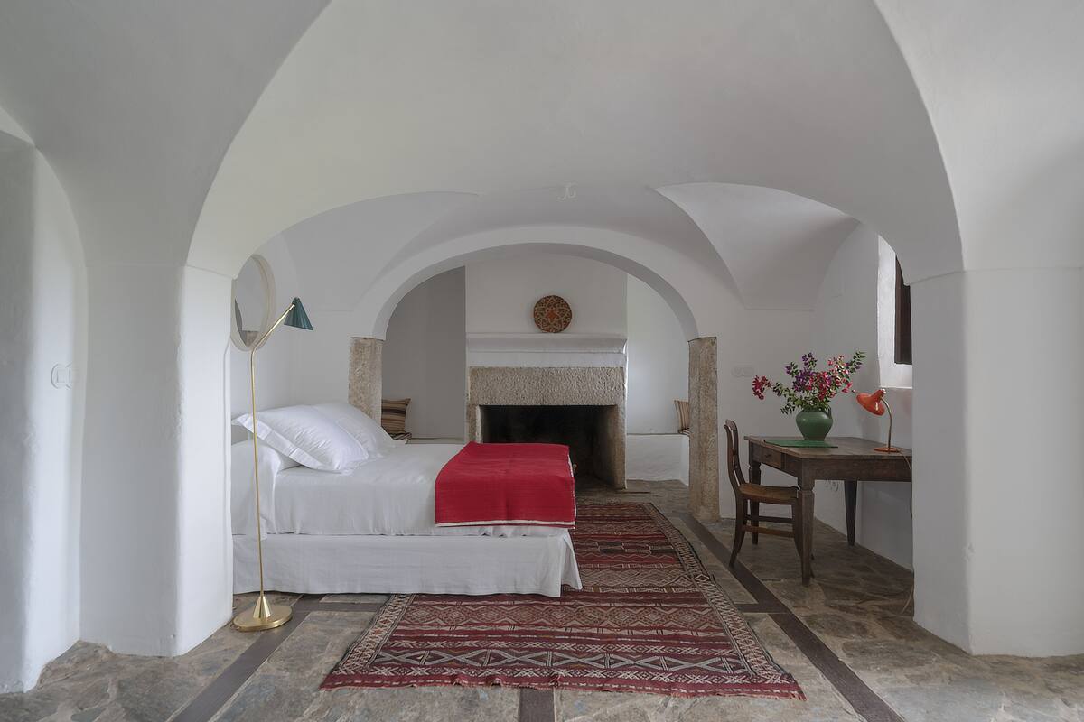Quarto com cama, lareira, escrivaninha e cadeira.