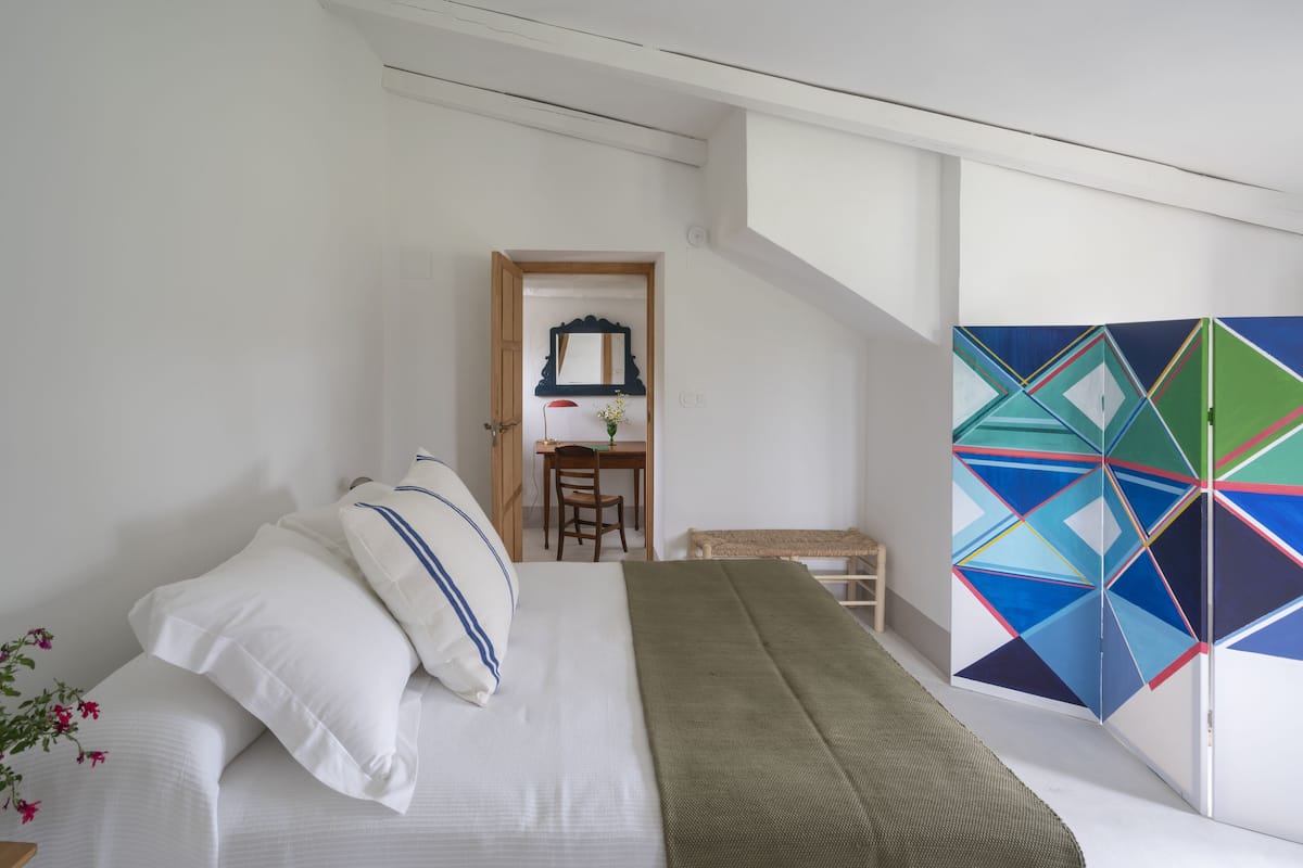 Quarto com cama, escrivaninha e arte de parede geométrica colorida.