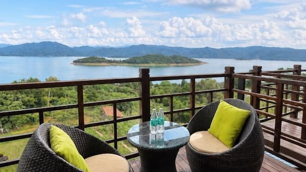 Uma varanda com cadeiras de vime e uma mesa, com vista para um lago e montanhas.