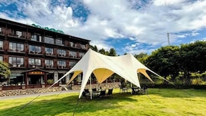 Um hotel com uma grande estrutura de tenda branca no pátio, um edifício de vários andares com varandas, e um céu claro.