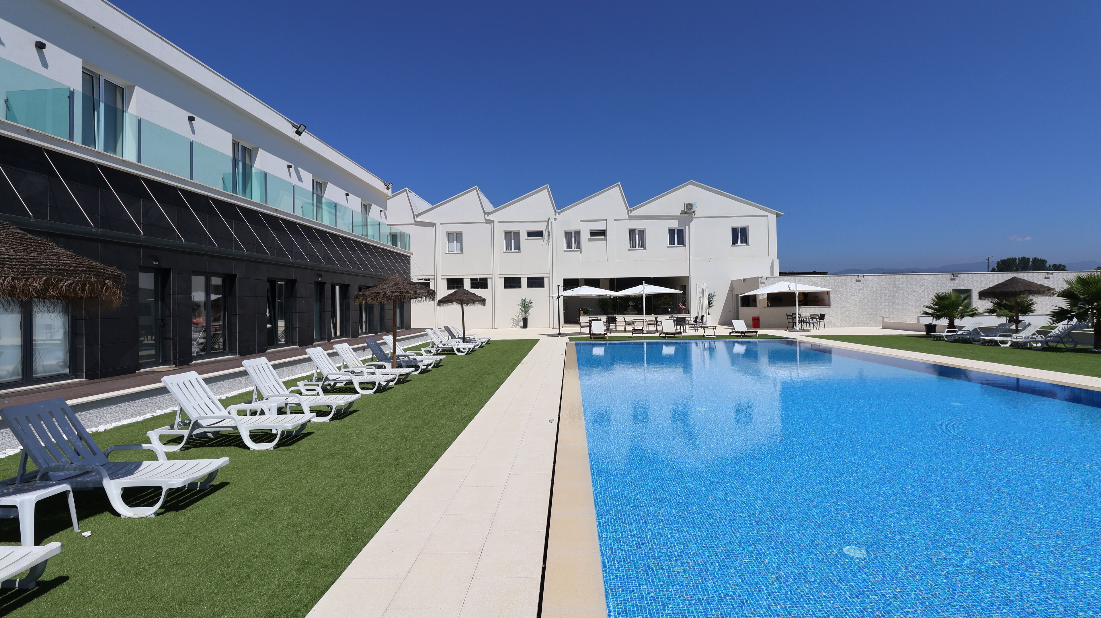 Um hotel moderno com piscina, espreguiçadeiras e um jardim bem cuidado.