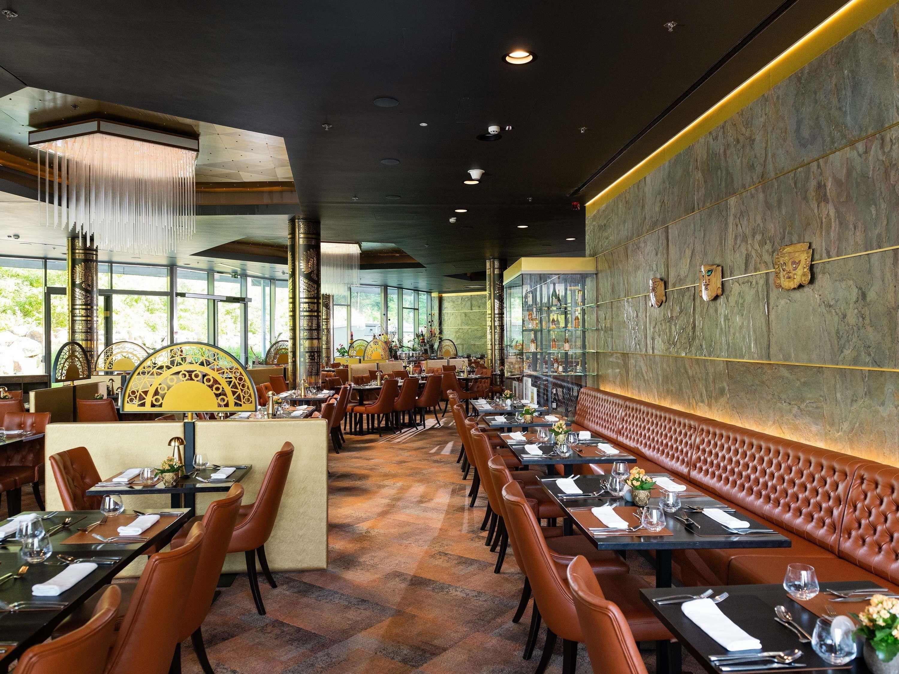Interior de restaurante com pé direito alto, iluminação moderna e área central com bancos estofados.