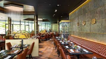 Interior de restaurante com pé direito alto, iluminação moderna e área central com bancos estofados.