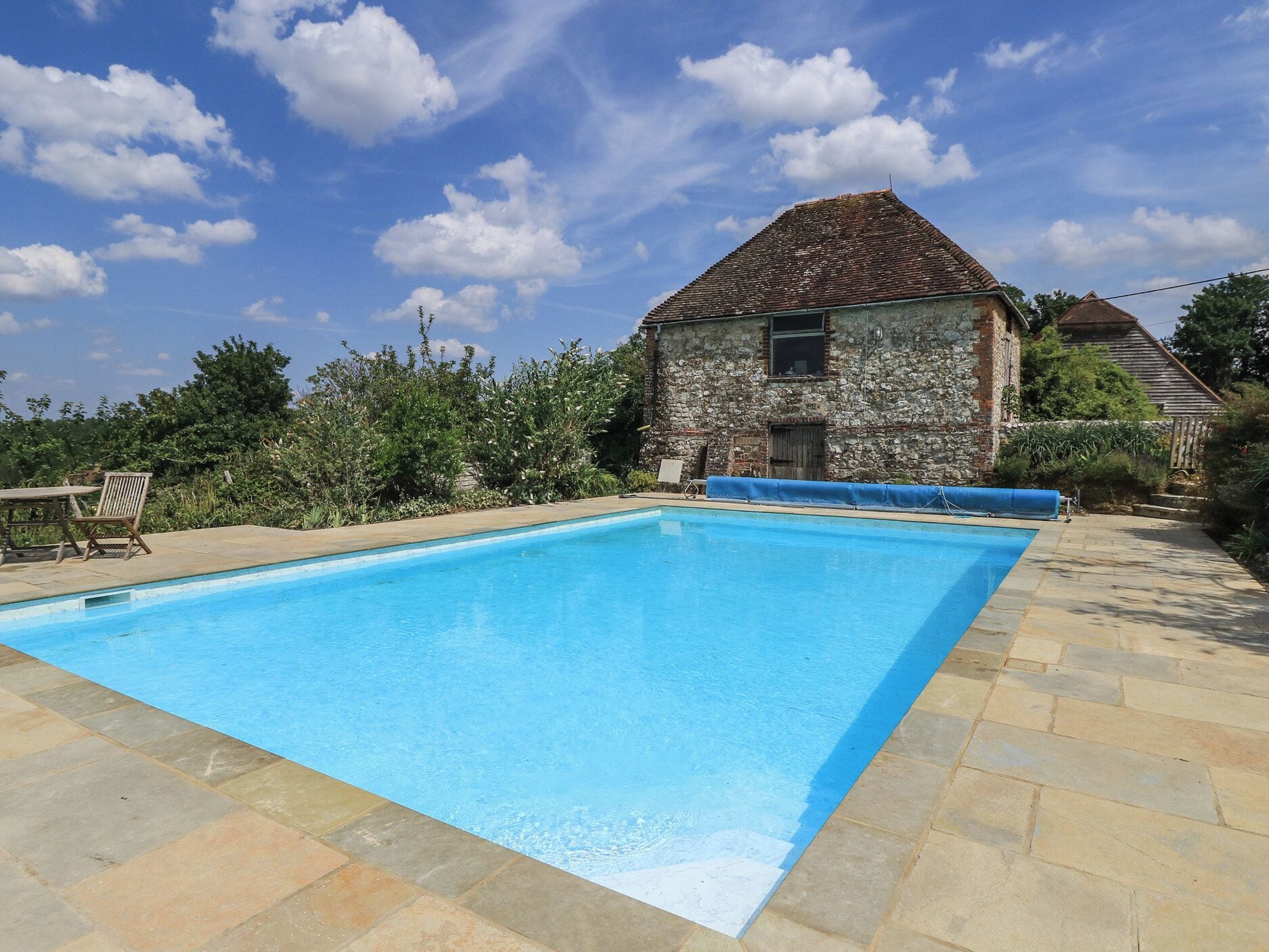 Piscina retangular com borda de pedra, rodeada por um pátio de pedra.