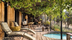 Um deck de madeira com espreguiçadeiras e piscina, cercado por vegetação e paredes de madeira.