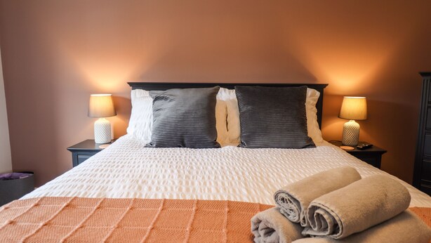 Uma cama bem arrumada com um edredom branco e laranja, duas almofadas e toalhas enroladas ao lado.