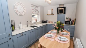 Uma cozinha moderna com armários cinza, uma mesa de jantar de madeira posta com jogos americanos rosa e um relógio decorativo na parede.