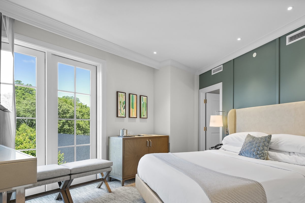 Quarto de hotel moderno com uma cama grande, uma escrivaninha e um banco perto da janela.