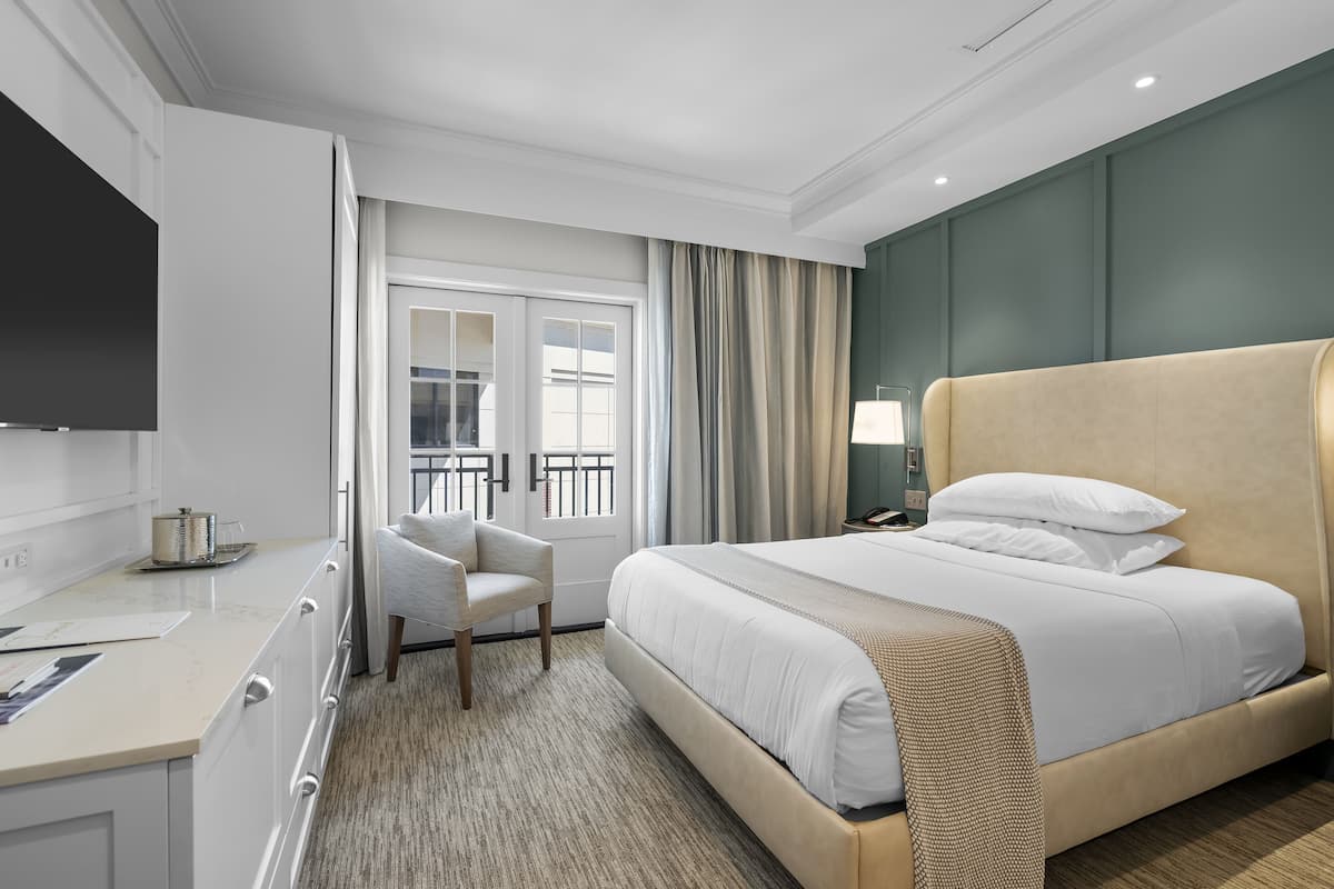 Quarto de hotel com uma cama, uma escrivaninha, uma cadeira, televisão e uma janela com cortinas.