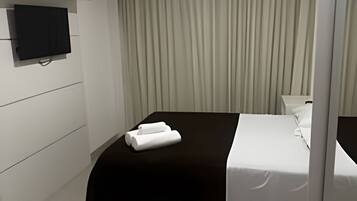 Quarto de hotel com cama, televisão de tela plana na parede e janela com cortinas.