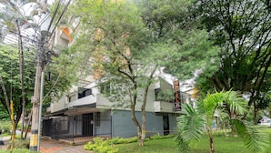 Edifício residencial com portão fechado, cercado por vegetação e um caminho pavimentado.