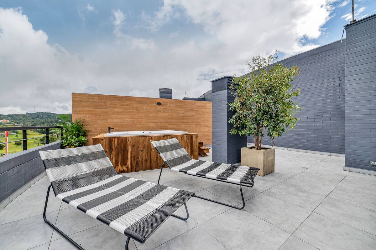 Terraço no telhado com duas cadeiras de descanso, um balcão de madeira e um vaso de planta.