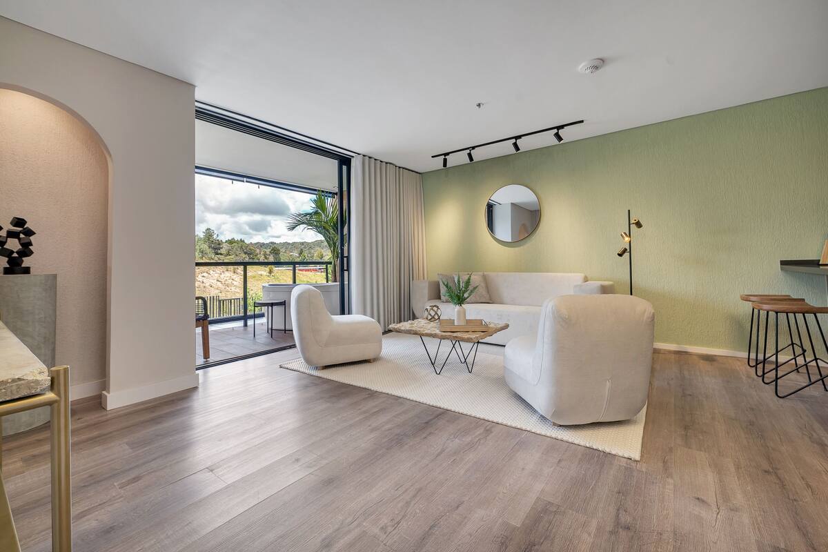 Uma sala de estar moderna com uma janela grande, um espelho redondo e uma área de estar com uma mesa de centro.