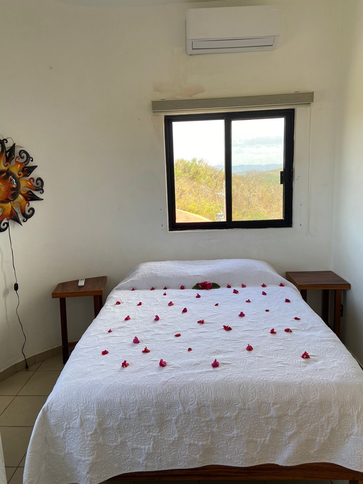 Quarto com cama, janela com vista para o verde, ar-condicionado fixado na parede e um objeto decorativo na parede.