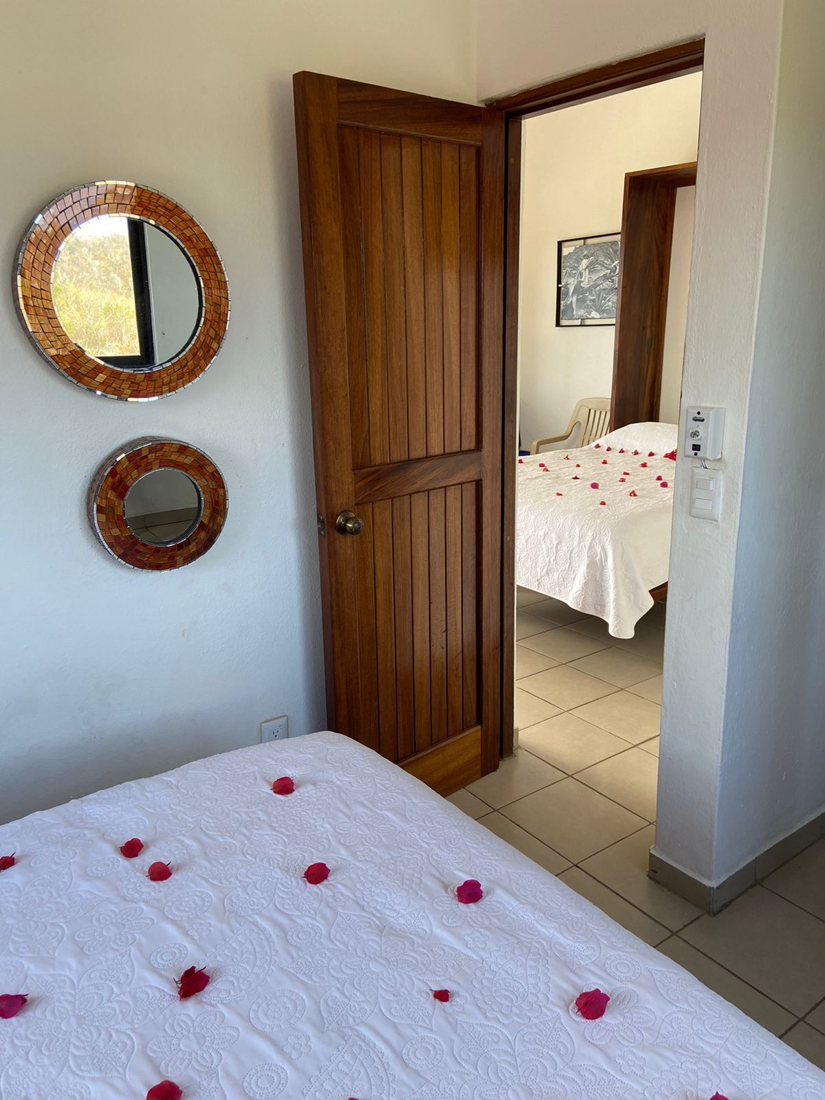 Quarto com cama, duas espelhos na parede e porta de acesso a outro cômodo.
