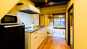Cozinha compacta com micro-ondas, fogão e pia. Em segundo plano, uma pequena área de refeições com uma mesa baixa e almofadas.