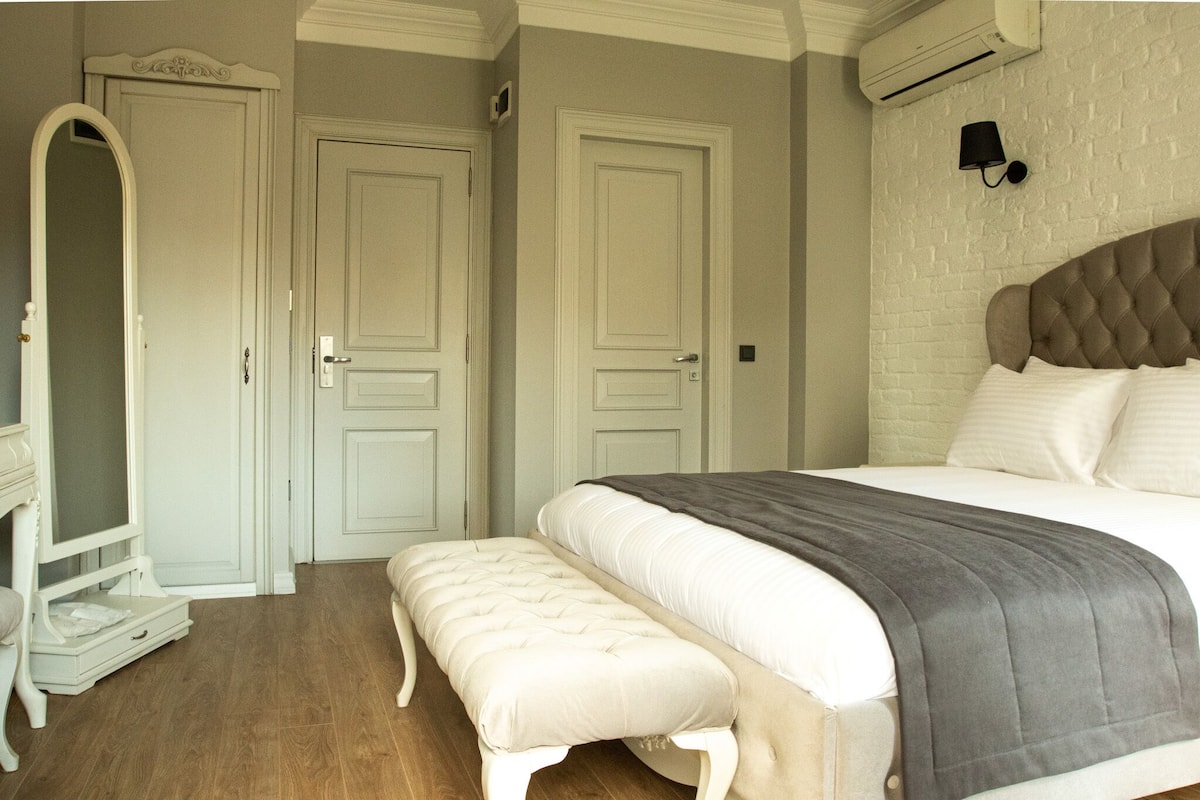 Quarto com uma cama grande, um banco, duas portas, uma cômoda e um luminário fixado na parede.