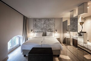 Quarto moderno com uma cama grande, cabeceira com textura, mesas de cabeceira com abajures, um espelho amplo e uma janela que traz luz natural.