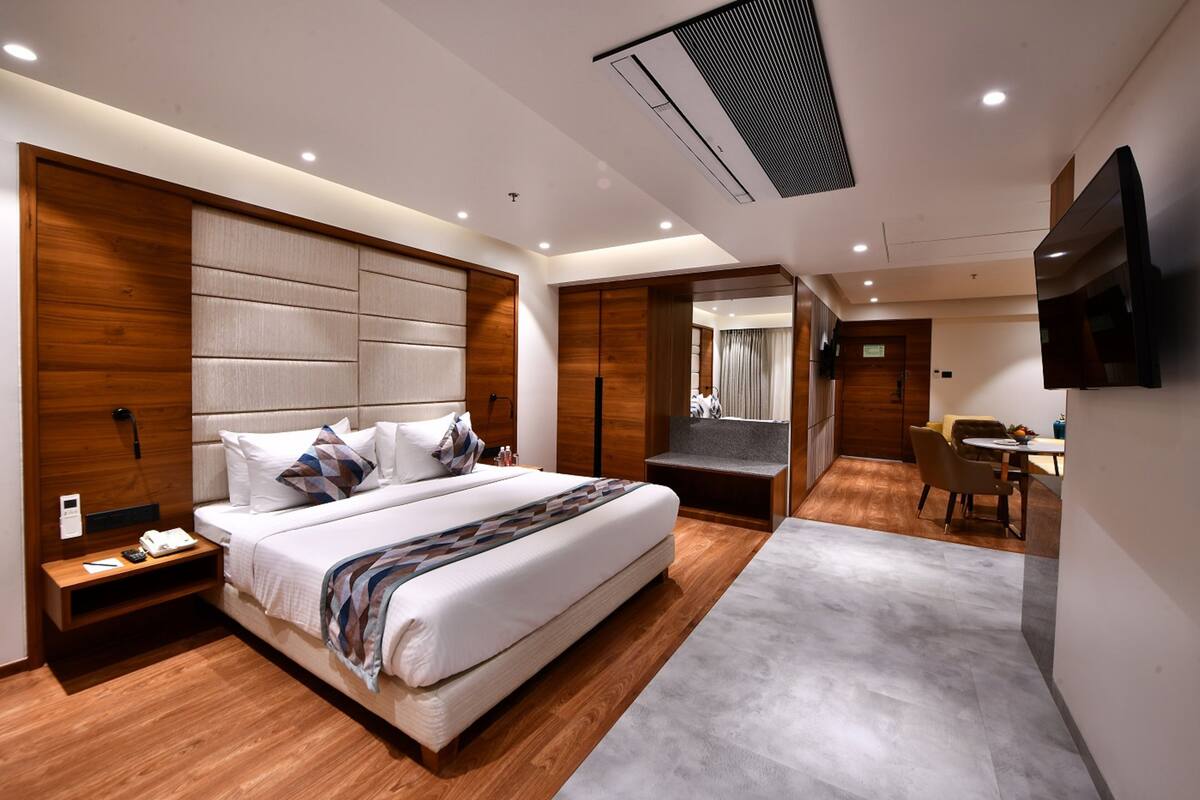 Quarto de hotel moderno com uma cama grande, cabeceira de madeira, mesas de cabeceira, uma escrivaninha e uma TV fixada na parede.