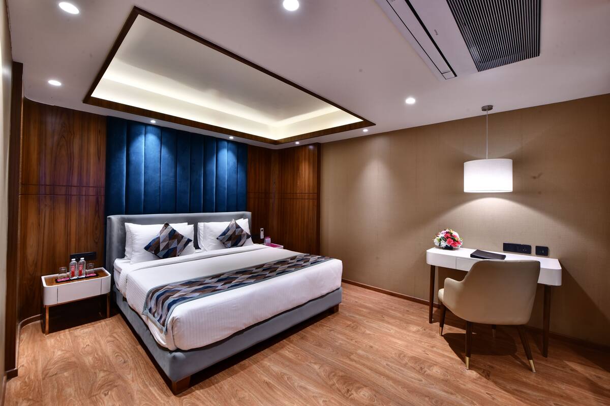 Quarto de hotel moderno com uma cama grande, mesas de cabeceira, escrivaninha e uma cadeira.