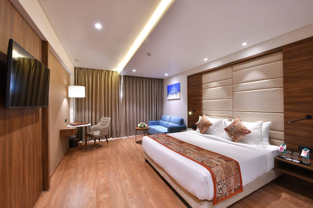 Quarto de hotel moderno com uma cama grande, escrivaninha, cadeira, sofá e televisão.