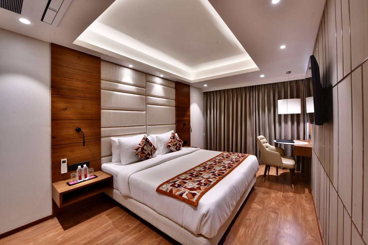Quarto de hotel moderno com uma cama grande, mesa de cabeceira e uma escrivaninha com cadeira.