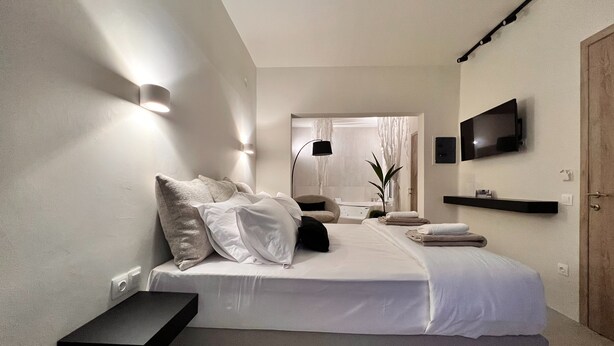 Quarto moderno com cama, mesas de cabeceira, televisão e banheiro visível por uma porta aberta.