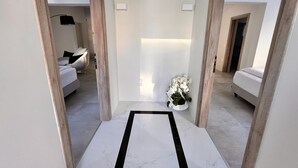 Quarto de hotel moderno com piso de mármore, arranjo central de flores brancas e cama com cabeceira branca.