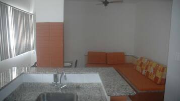 Cozinha com bancada de granito, pia e sofá laranja embutido com almofadas estampadas.